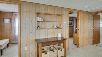 Quarto com paredes de painel de madeira, uma escrivaninha de madeira com espelho, um banco e cestos de vime.