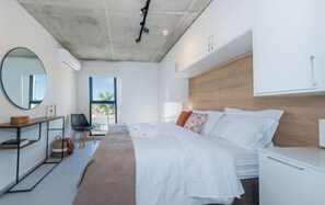 Quarto moderno com cama grande, mesa de cabeceira, espelho e vista para o exterior.