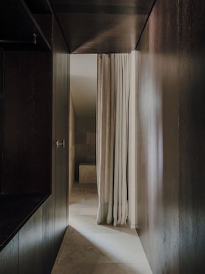 Um corredor com porta de madeira, cortina e um banco ao fundo.