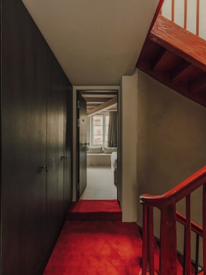 Corredor que dá acesso a um quarto com carpete vermelho, escada de madeira e um guarda-roupa.