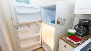 Cozinha com geladeira aberta, cafeteira e uma tigela pequena verde no balcão.