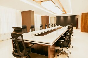 Sala de conferência com uma mesa comprida, cadeiras pretas e uma parede de destaque em madeira.