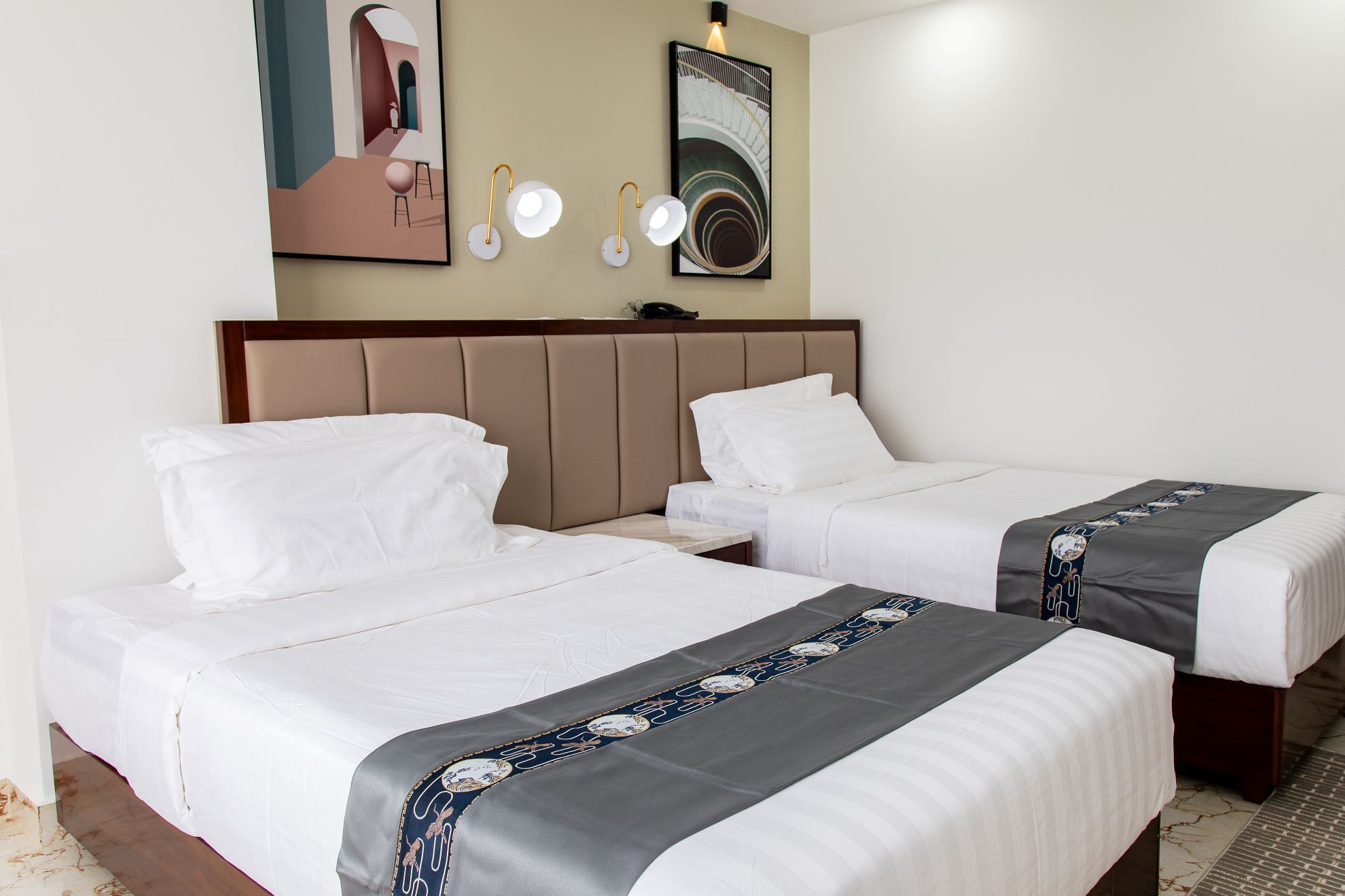 Quarto de hotel com duas camas, cabeceira e obras de arte na parede.