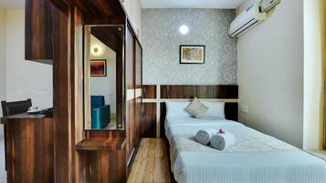 Quarto de hotel com escrivaninha de madeira, cama com roupa de cama branca e ar-condicionado fixado na parede.