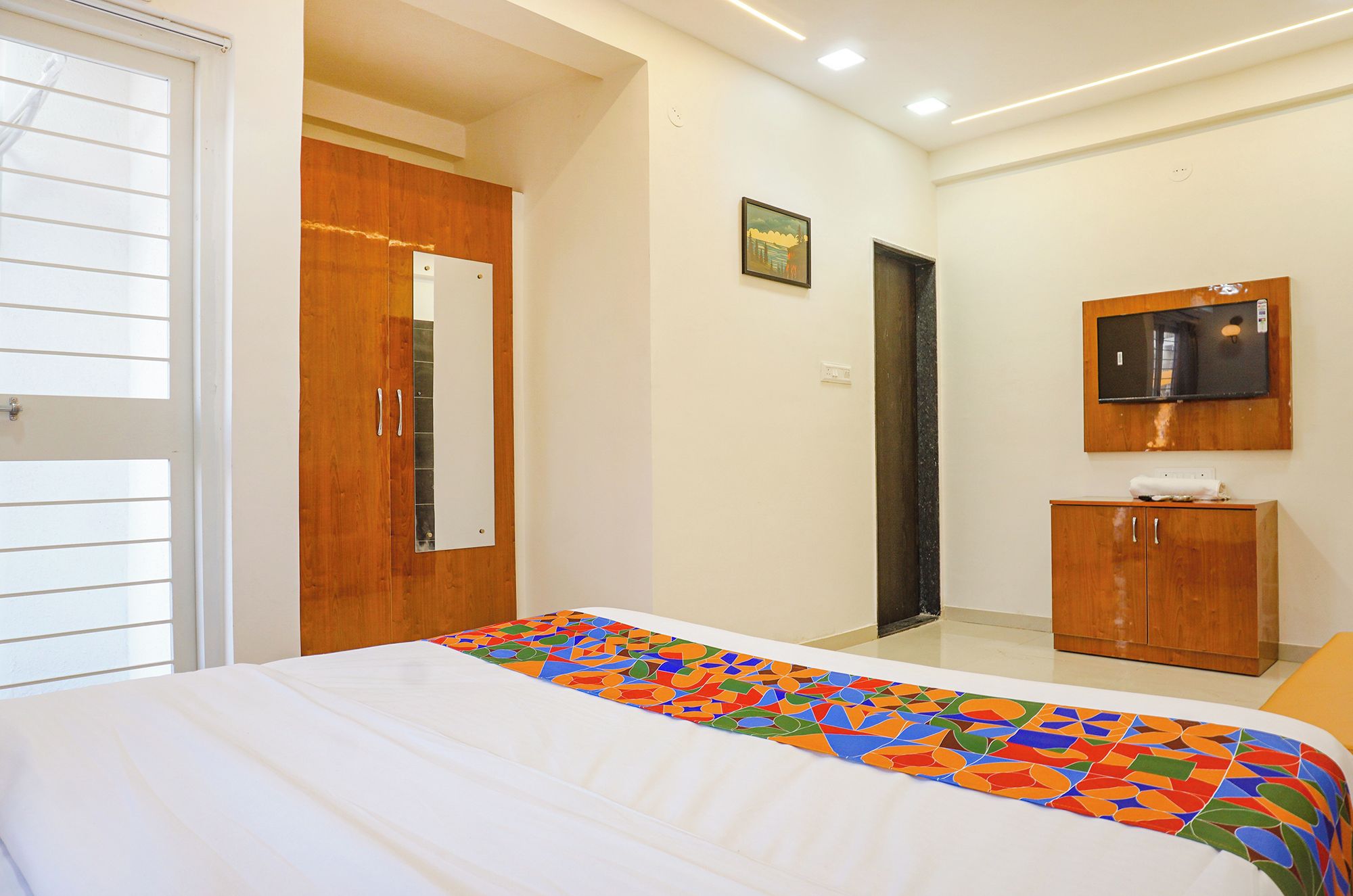 Quarto com uma cama, um guarda-roupa de madeira, uma televisão e uma porta.