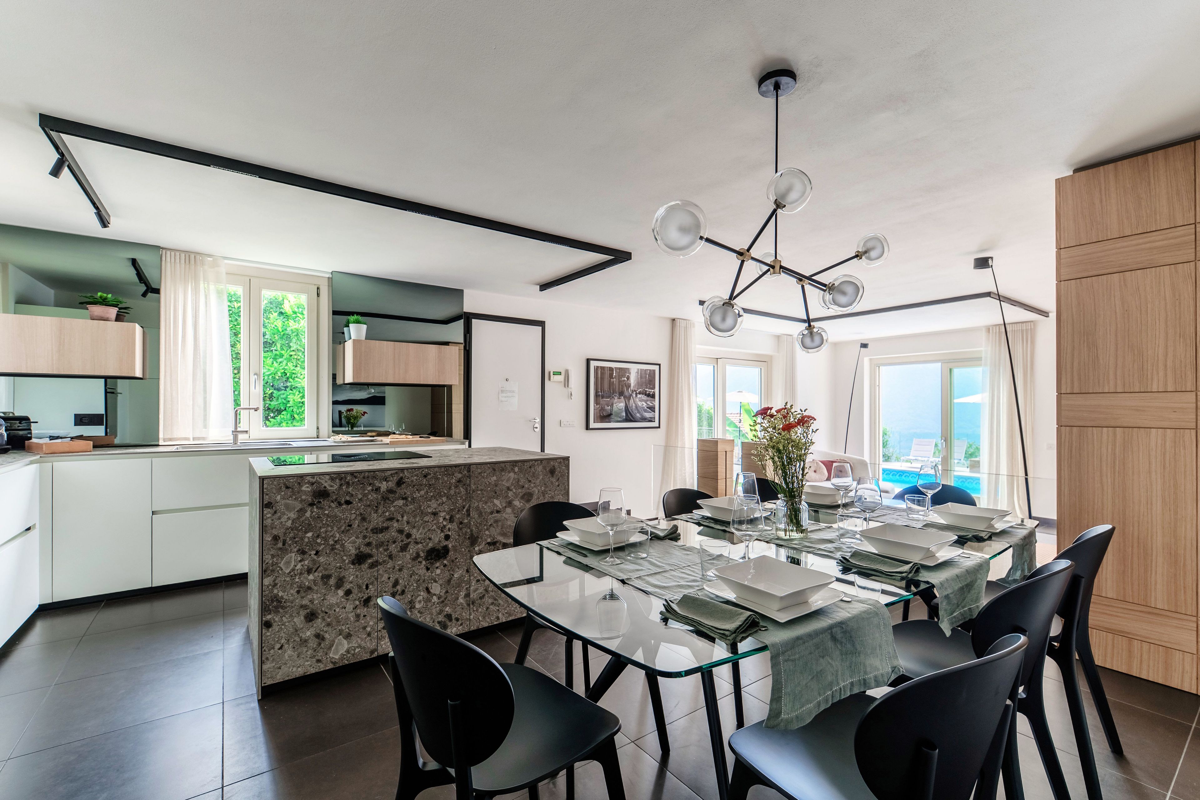 Cozinha moderna com ilha central, área de refeições com cadeiras e vista para o exterior.