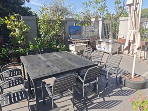 Pátio externo com mesa e cadeiras, cercado por vegetação e um portão decorativo.