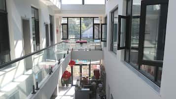 Interior com vários níveis, corrimãos de vidro, escadaria central e vista para o exterior.