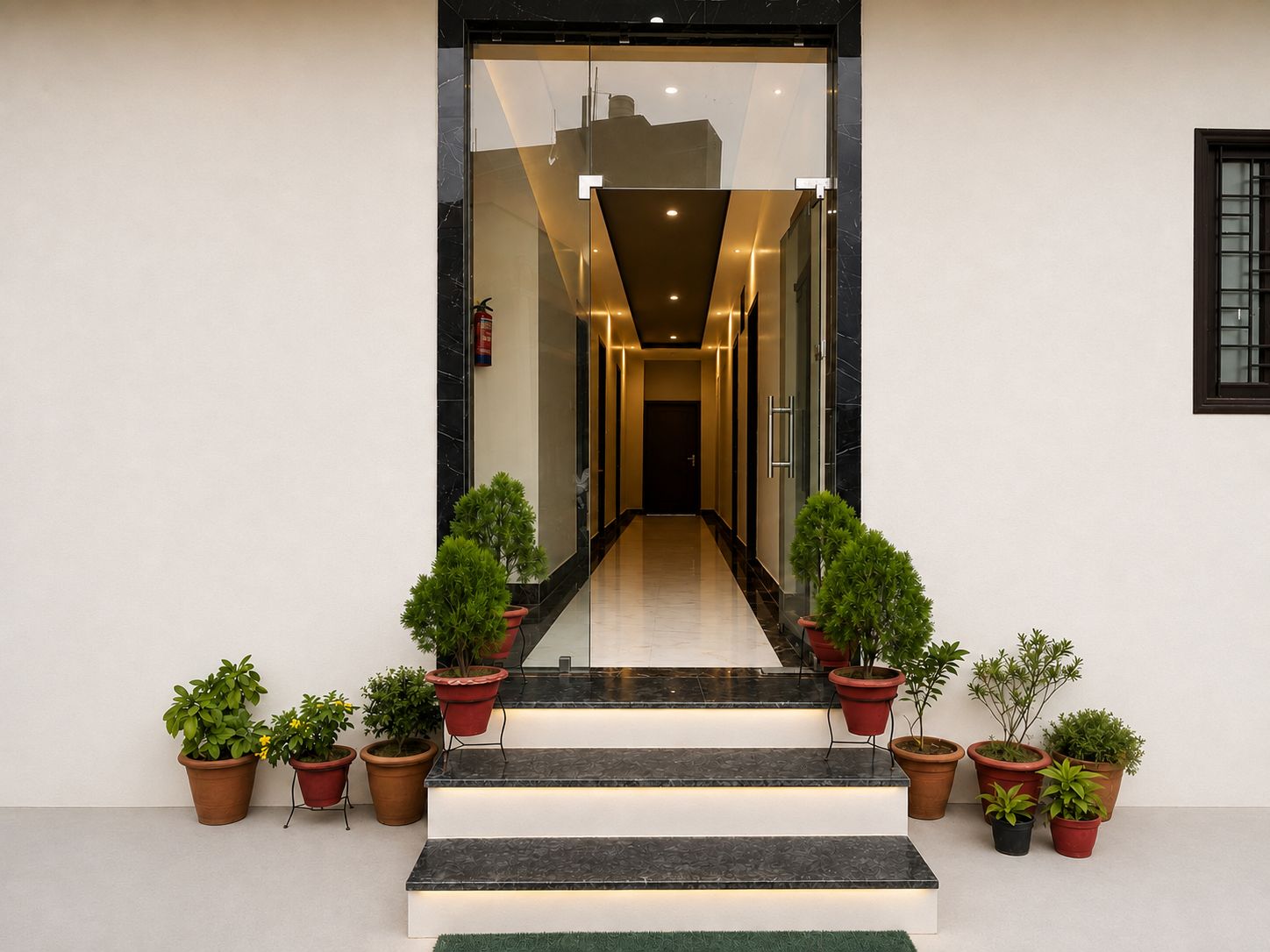 Uma entrada moderna com porta de vidro, escadaria de mármore e plantas em vasos.