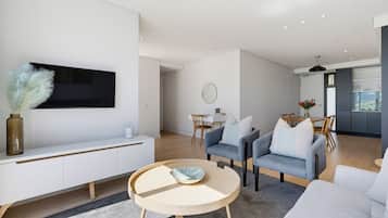 Uma sala de estar moderna com televisão de tela plana, sofá, mesa de centro e área de jantar com mesa e cadeiras.