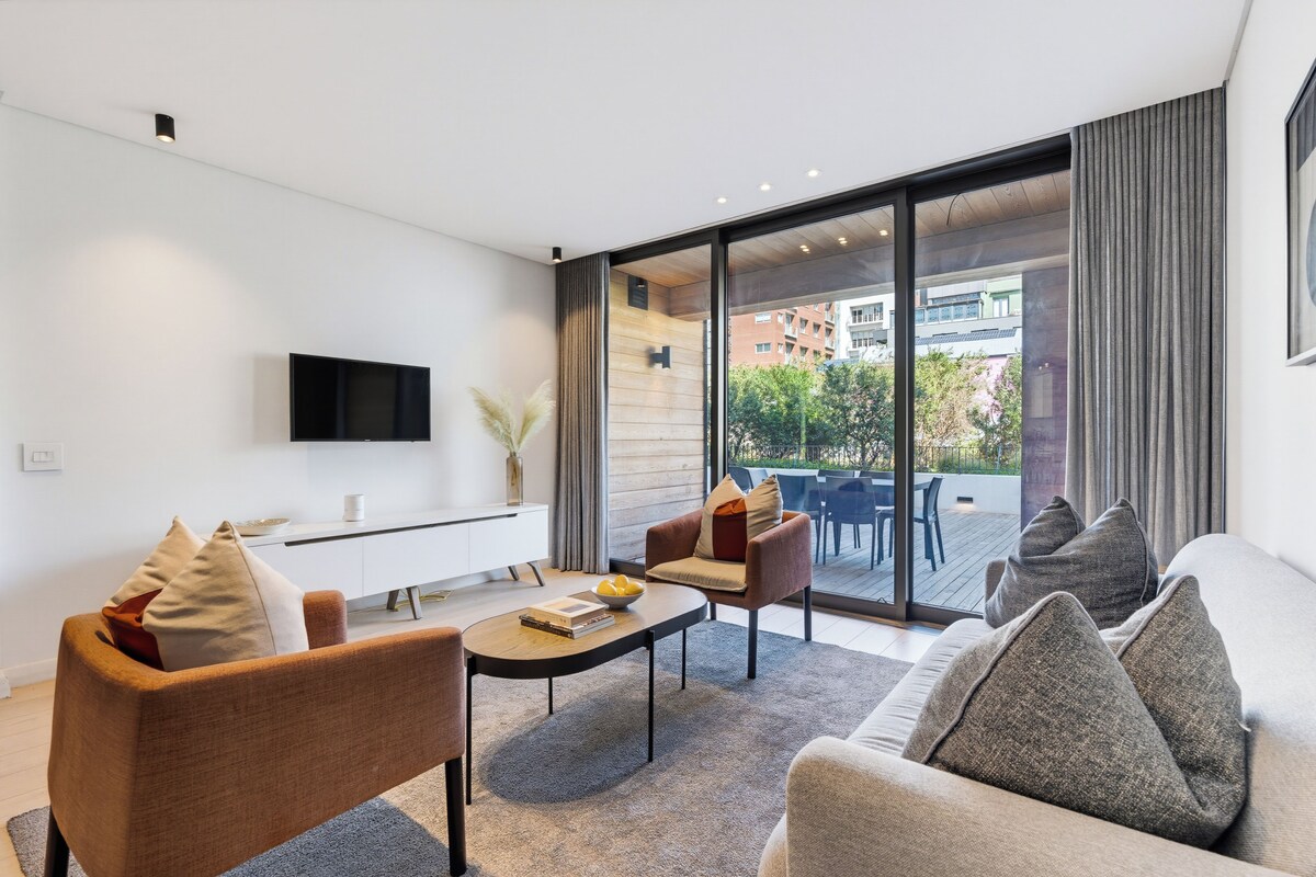 Uma sala de estar moderna com televisão de tela plana, um sofá, uma mesa de centro e um espaço de jantar com cadeiras.