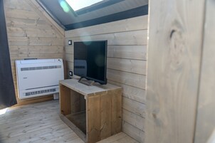 Quarto com parede de madeira, televisão sobre suporte de madeira e aparelho de ar condicionado.