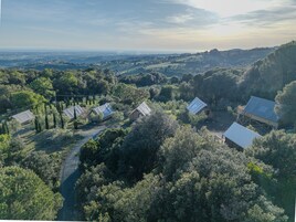 Paisagem rural com vários edifícios rodeados por vegetação densa e colinas ao fundo.