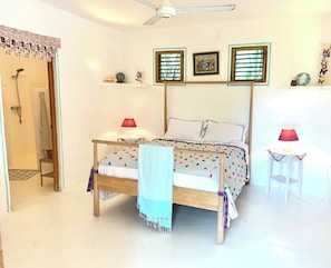 Quarto com cama de madeira, duas mesas de cabeceira com luminárias, ventoinha no teto e área de chuveiro.