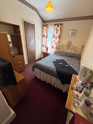 Quarto com cama, guarda-roupa, escrivaninha com cadeira, mesa de cabeceira e janela com cortinas.