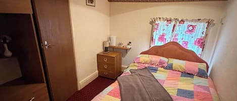 Quarto com cama, guarda-roupa, mesa de cabeceira, luminária, janela com cortinas e luz no teto.