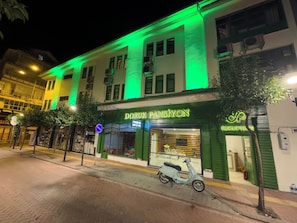 Um edifício com fachada iluminada em verde, com a placa 'DORUK PANSIYON' e uma scooter estacionada em frente.