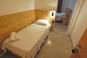Uma cama de solteiro com cabeceira de madeira, mesa de cabeceira e luminária fixada na parede.