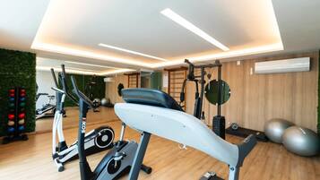 Academia com equipamentos de exercício, parede verde e piso de madeira.