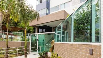 Um edifício moderno com fachada de vidro, exterior em tijolo e área ajardinada com palmeiras e plantas.