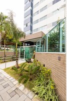 Um edifício moderno com fachada de vidro, exterior em tijolo e área ajardinada com palmeiras e plantas.