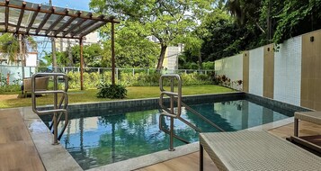 Piscina com grades de metal, área de estar coberta e jardim com grama e plantas.