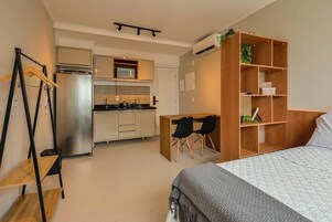Um apartamento estúdio compacto com cozinha compacta, uma cama, escrivaninha e guarda-roupa.