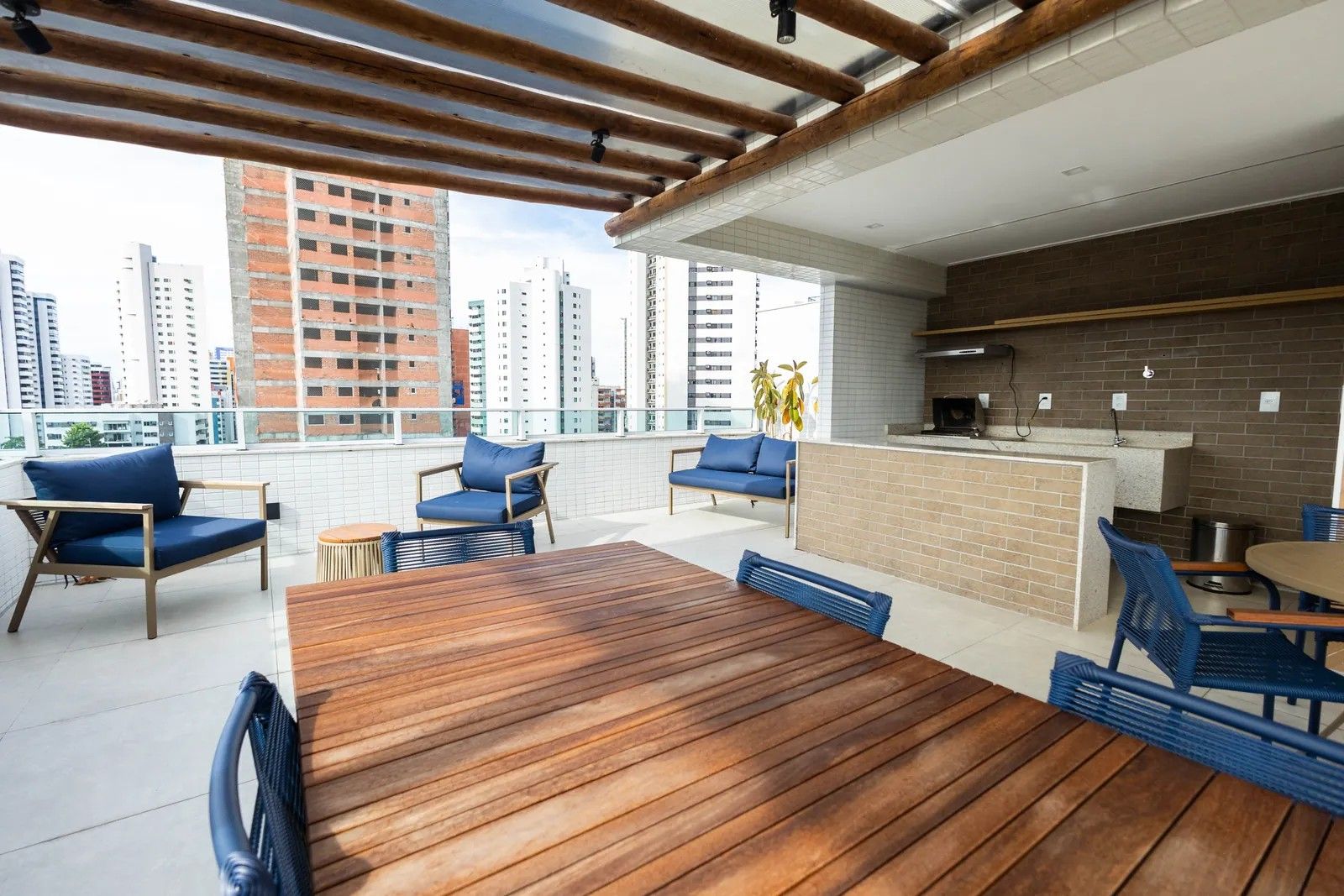 Terraço no telhado com mesa de madeira, cadeiras azuis, área de bar e vista para a cidade.