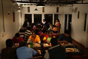 Restaurante com várias mesas e cadeiras, clientes jantando e algumas pessoas em pé.