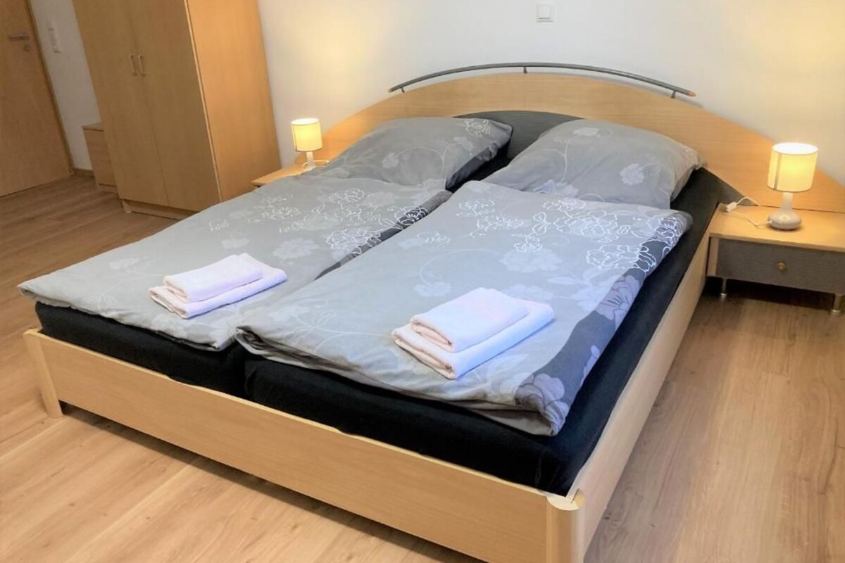 Uma cama de casal com estrutura de madeira, duas mesas de cabeceira com abajures e um guarda-roupa ao fundo.