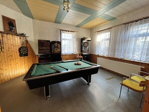 Mesa de bilhar em um espaço com lambris, alvo de dardos e máquina de pinball.