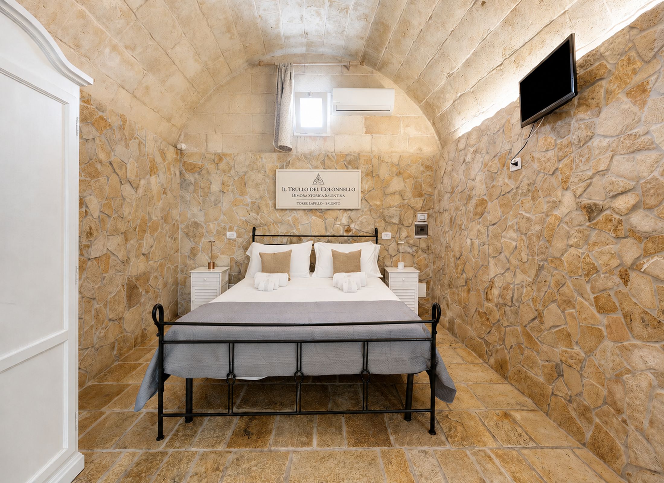 Quarto com paredes de pedra, uma cama, mesas de cabeceira e um ar condicionado.