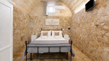 Quarto com paredes de pedra, uma cama, mesas de cabeceira e um ar condicionado.