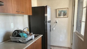 Cozinha compacta com armários de madeira, geladeira de aço inoxidável e escorredor de louça no balcão.