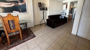 Uma sala de estar com um sofá de cor escura, uma cadeira de madeira, uma mesa pequena e um quadro na parede.