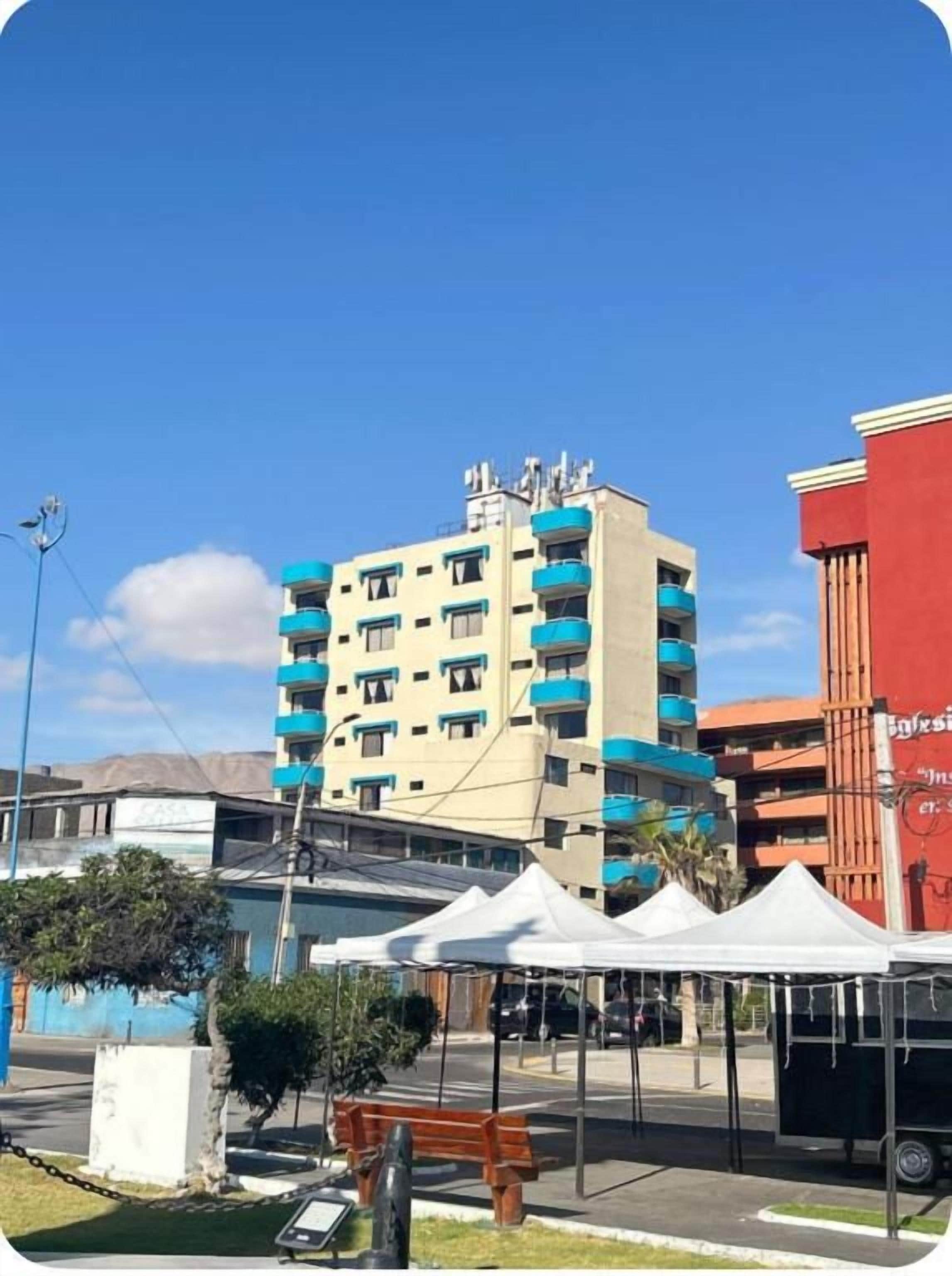 Um edifício com vários andares e varandas, com uma rua em frente e uma estrutura de tenda branca.