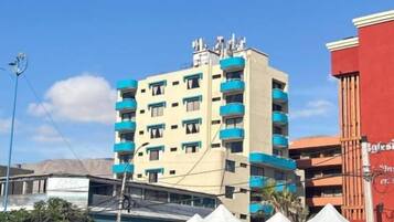 Um edifício com vários andares e varandas, com uma rua em frente e uma estrutura de tenda branca.