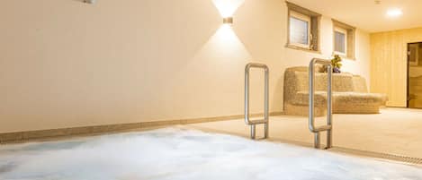 Uma área de spa com uma banheira de hidromassagem, um espaço de estar com um banco acolchoado e um espelho fixado na parede.
