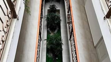 Corredor com um vaso de plantas central e paredes brancas, ladeado por grades de metal.
