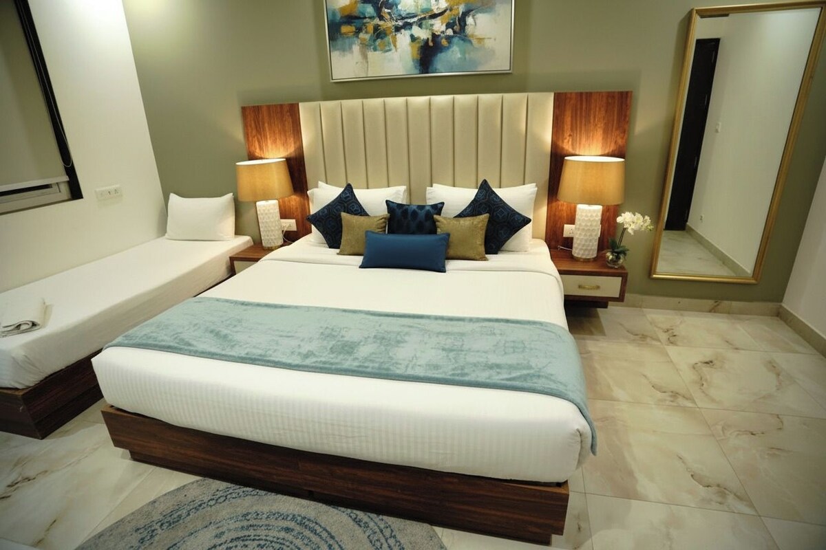 Quarto de hotel com uma cama grande, duas mesas de cabeceira com luminárias, um espelho e um quadro na parede.