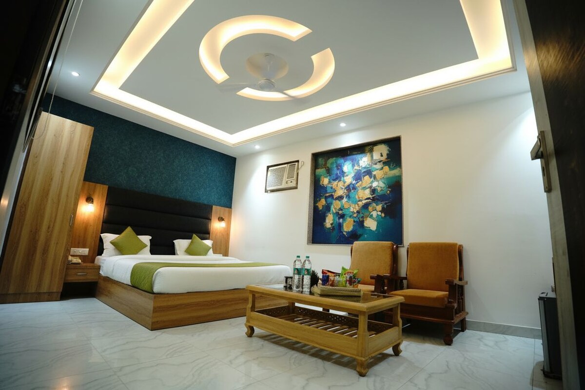 Quarto de hotel moderno com uma cama, uma mesa de centro, uma cadeira e um quadro na parede.