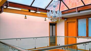 Um interior em vários níveis, com guarda-corpo de vidro, um candelabro e uma porta de madeira.