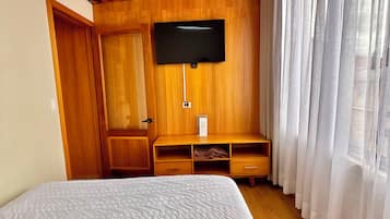 Quarto com cama, televisão na parede, guarda-roupa de madeira e janela com cortinas.