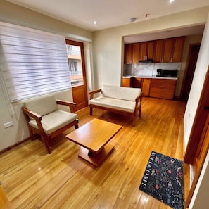 Um espaço de estar compacto com cozinha compacta, piso de madeira e área de estar com dois sofás e uma mesa de centro.