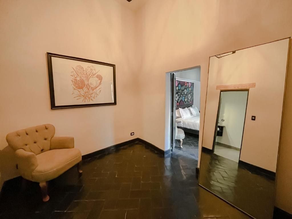 Quarto com piso de azulejos escuros, uma obra de arte emoldurada na parede, uma poltrona bege e um espelho refletindo parte do espaço.