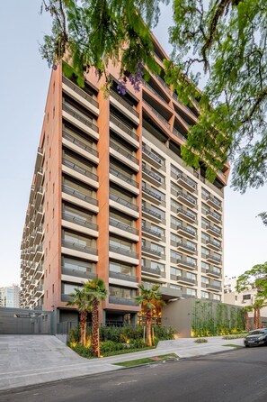 Um edifício residencial com vários andares, varandas e um jardim frontal ajardinado.