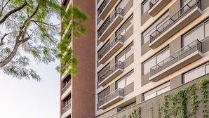 Um edifício moderno com telhado plano, várias varandas e uma parede coberta por plantas trepadeiras.
