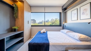 Quarto moderno com uma janela ampla, uma cama, um banco e prateleira na parede com plantas.