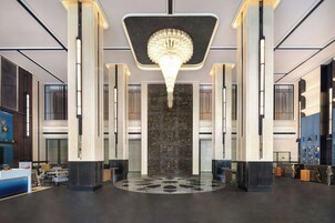 Um hall amplo com um lustre central, tetos altos e um piso com padrão circular.