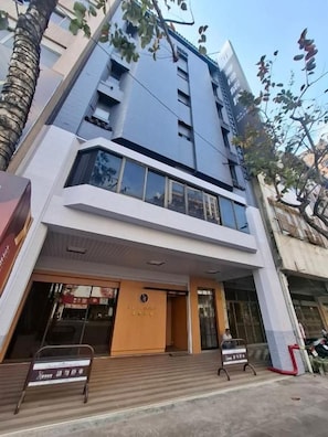 Um edifício moderno com entrada destacada, grandes janelas e uma placa indicando um hotel.